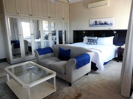 Quarto de hotel com cama, sofá, mesa de centro de vidro e guarda-roupa com espelhos.