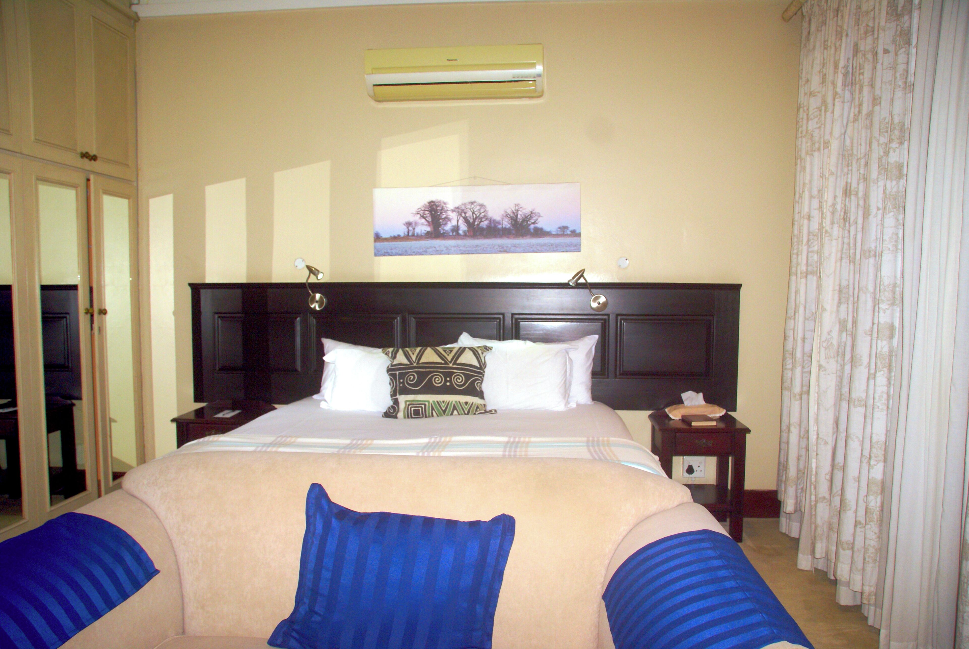Quarto de hotel com uma cama grande, mesa de cabeceira e espelho, além de janela com cortinas.