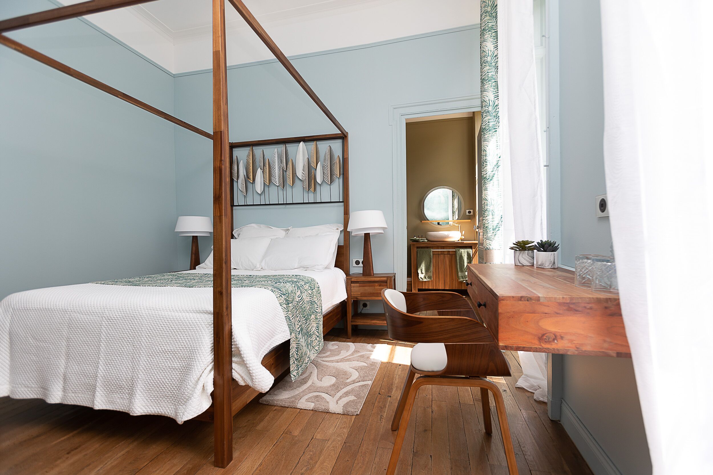 Quarto com cama de dossel, escrivaninha de madeira, toucador com espelho e uma pequena planta na escrivaninha.
