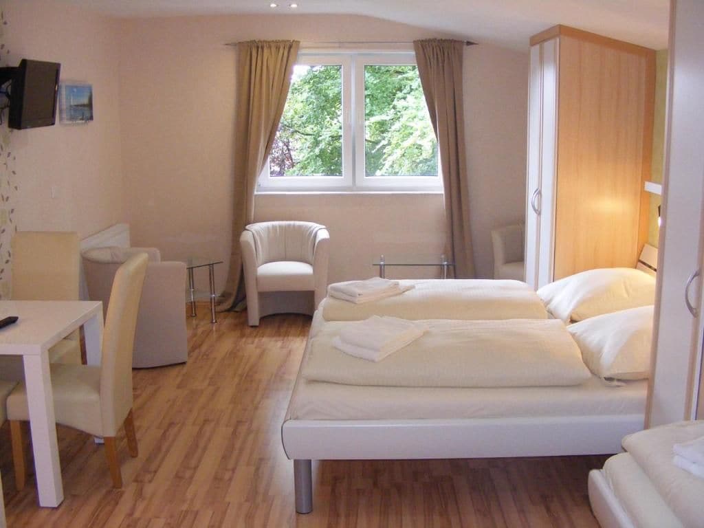 Quarto de hotel com cama, cadeira, escrivaninha e janela com cortinas.