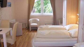 Quarto de hotel com cama, cadeira, escrivaninha e janela com cortinas.