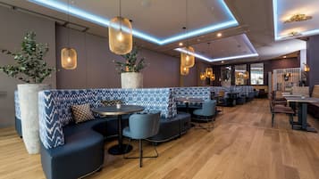Um restaurante moderno com piso de madeira, assentos estampados em azul e branco, luminárias pendentes e plantas em vasos.