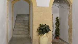 Um corredor com escadaria de pedra, um vaso grande e plantas em vasos.