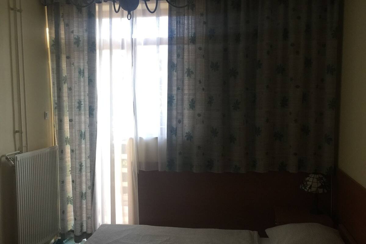 Quarto de hotel com cama, radiador, candelabro e cortinas.