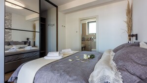 Quarto moderno com uma cama grande, mesa de cabeceira, espelho e vista para o banheiro.