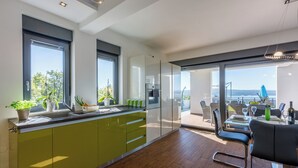 Uma cozinha moderna com armários verdes, uma janela ampla e uma área de jantar com vista para o mar.