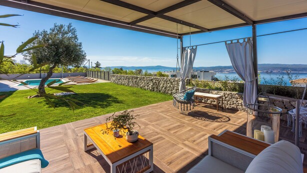 Um alpendre coberto com vista para o mar, uma piscina e uma área gramada com móveis de exterior.