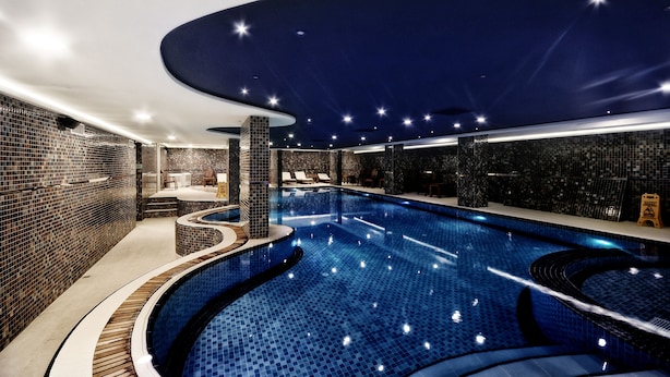 Uma piscina interior moderna com design curvo, paredes revestidas e teto estrelado.