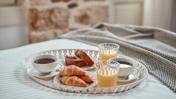 Bandeja de café da manhã com croissants, café e suco de laranja sobre uma cama com colcha listrada.