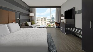 Quarto de hotel moderno com uma cama grande, uma escrivaninha, televisão e vista para a cidade.