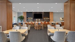 Uma sala de conferências moderna com várias mesas e cadeiras, uma TV de tela plana grande e um espaço bar com prateleiras cheias de garrafas.