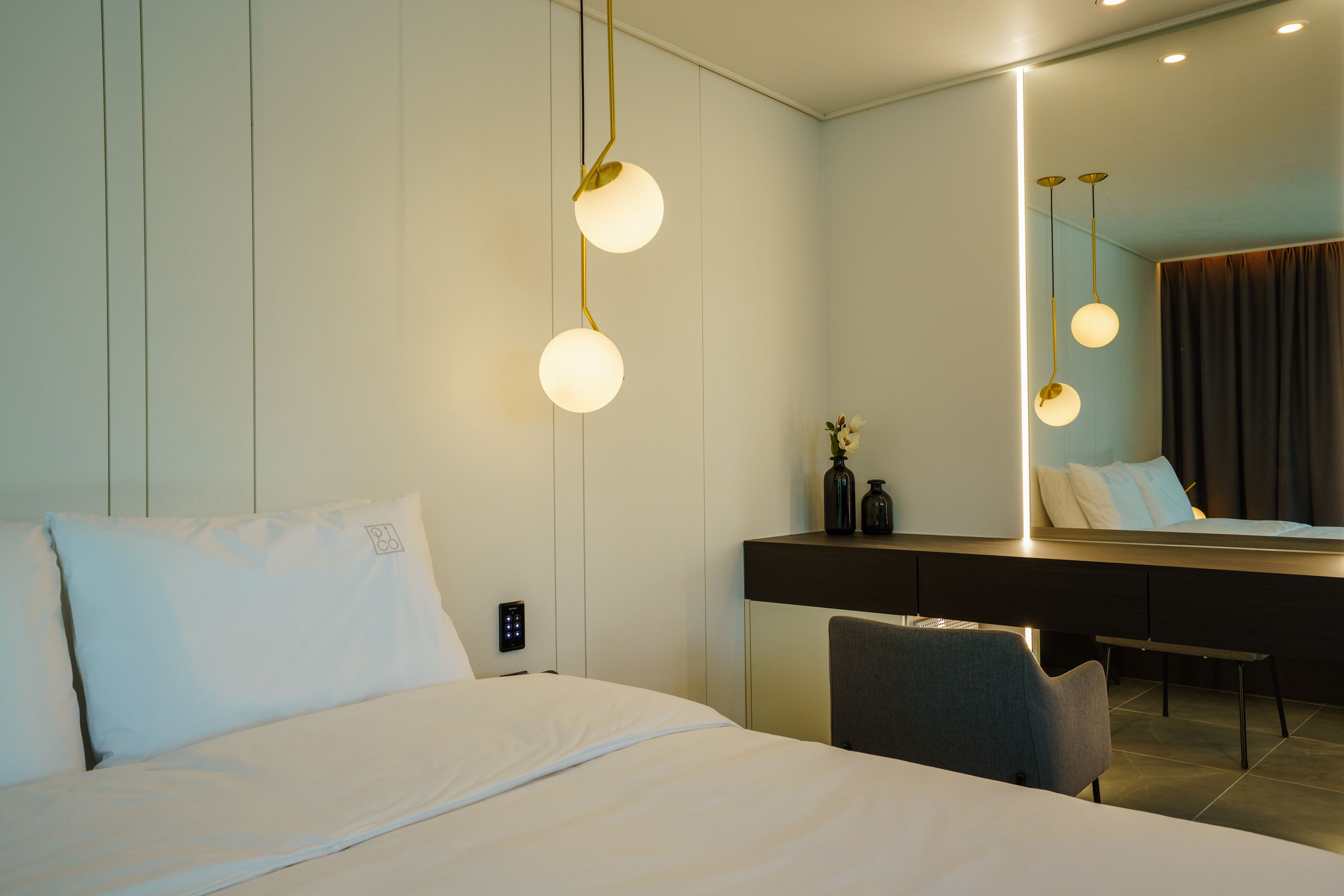 Quarto de hotel moderno com cama bem arrumada, escrivaninha com cadeira e um espelho grande refletindo o quarto.