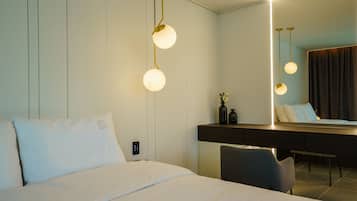 Quarto de hotel moderno com cama bem arrumada, escrivaninha com cadeira e um espelho grande refletindo o quarto.
