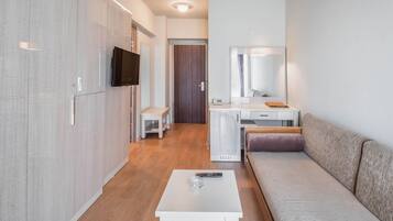 Quarto moderno e bem iluminado, com sofá, uma mesa pequena, TV fixada na parede e espelho sobre a escrivaninha.