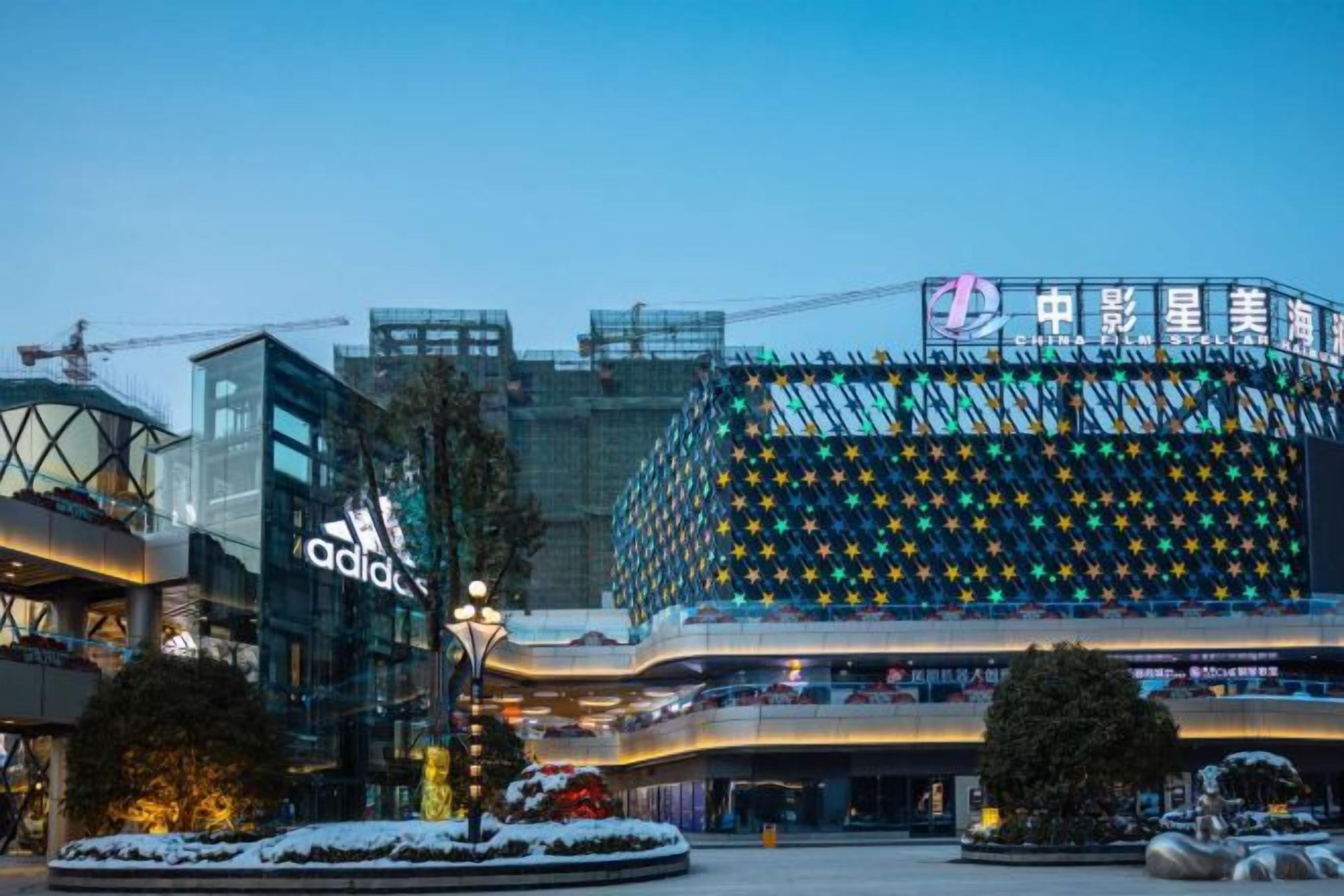 Um edifício moderno com fachada em padrão de estrela, um sinal Adidas bem visível e uma grande placa iluminada no topo.