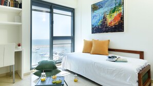 Quarto de hotel com uma cama, uma mesa com itens de café da manhã, vista para o mar e uma estante com livros.