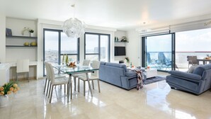 Uma sala de estar moderna com uma mesa de jantar de vidro, dois sofás e uma janela grande com vista para a cidade.