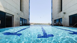 Piscina com água azul cristalina, cercada por um edifício com janelas e portas amplas.