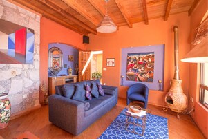 Uma sala de estar acolhedora com um sofá, uma poltrona, um vaso decorativo e um fogão rústico.