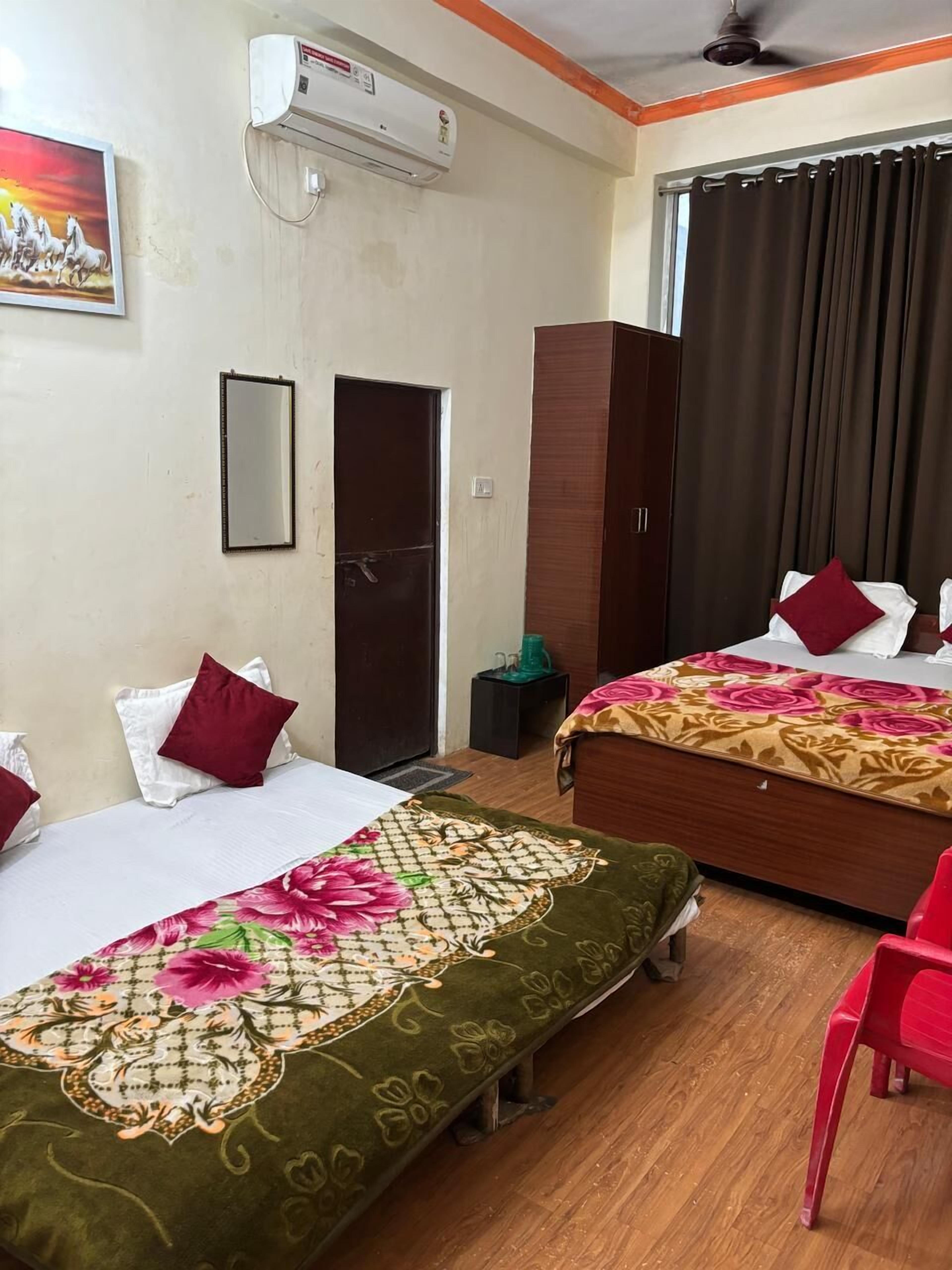 Quarto de hotel com duas camas, um guarda-roupa, ar condicionado, espelho e janela com cortinas.
