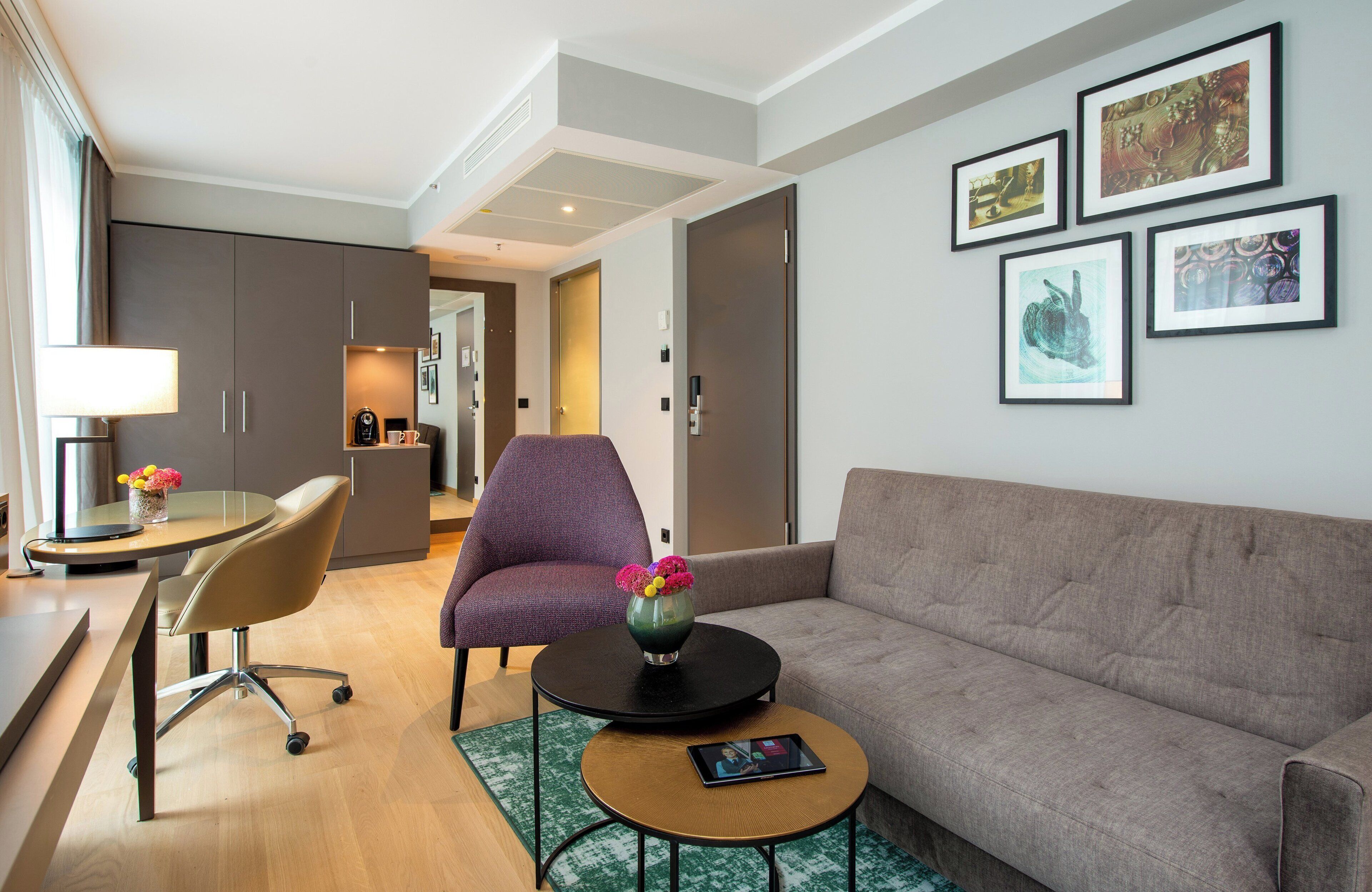 Quarto de hotel moderno com sofá, poltrona, mesa de jantar e uma mesinha de centro com um vaso de flores.