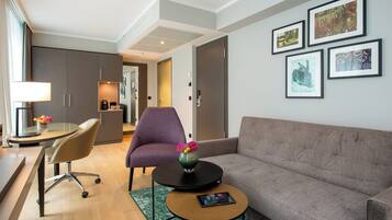 Quarto de hotel moderno com sofá, poltrona, mesa de jantar e uma mesinha de centro com um vaso de flores.