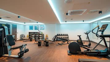 Uma academia moderna com diversos equipamentos de exercício, piso de madeira e área de estar com sofá e cadeiras.