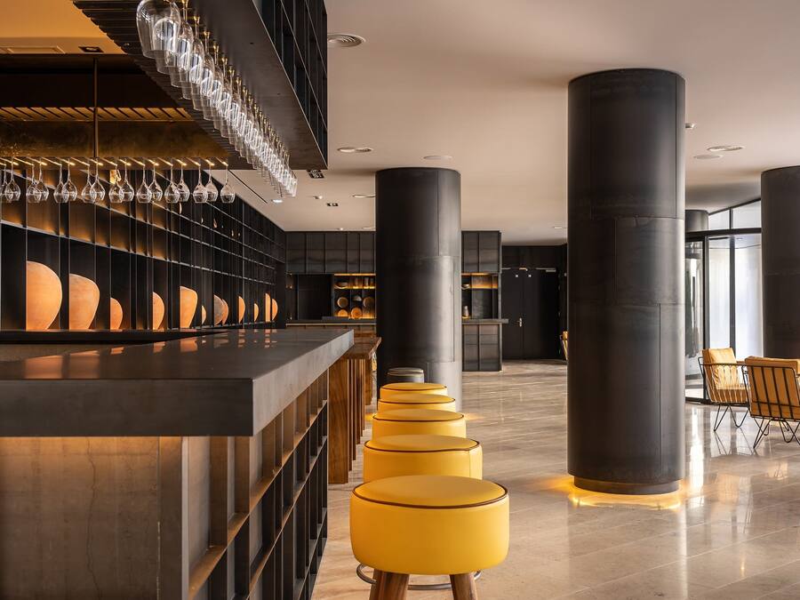 Uma área de bar moderna com um balcão extenso, vários bancos e um lustre diferenciado.