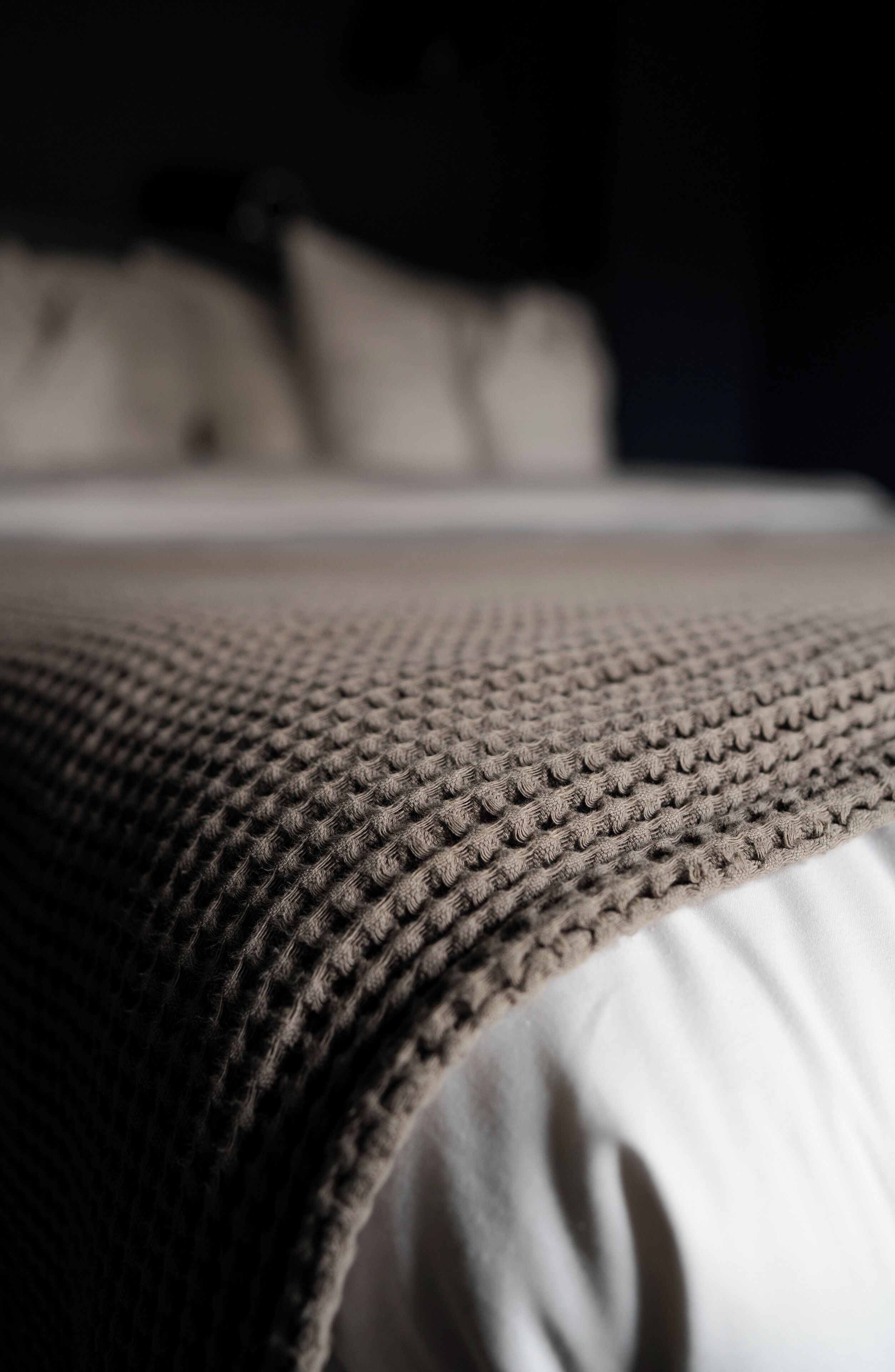 Close-up de um tecido texturizado, provavelmente parte de uma cama ou área de assentos, com um fundo desfocado que sugere um ambiente interno.
