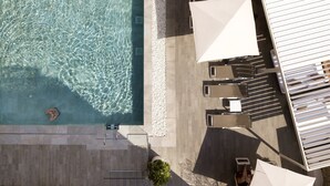 Vista aérea de uma piscina com água cristalina, cercada por espreguiçadeiras e guarda-sóis, indicando um ambiente de resort.