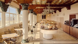 Um hall de hotel espaçoso, com pé-direito alto, amplas janelas e um balcão de bar central.