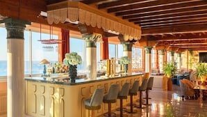 Uma área de bar com vista para o oceano, banquetas e um balcão com garrafas.