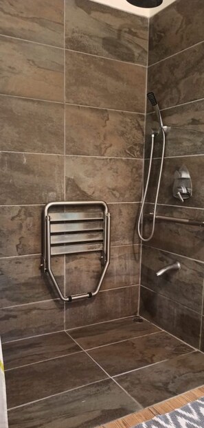 Área de chuveiro com chuveiro de metal, um chuveiro manual e um porta-toalhas de metal.