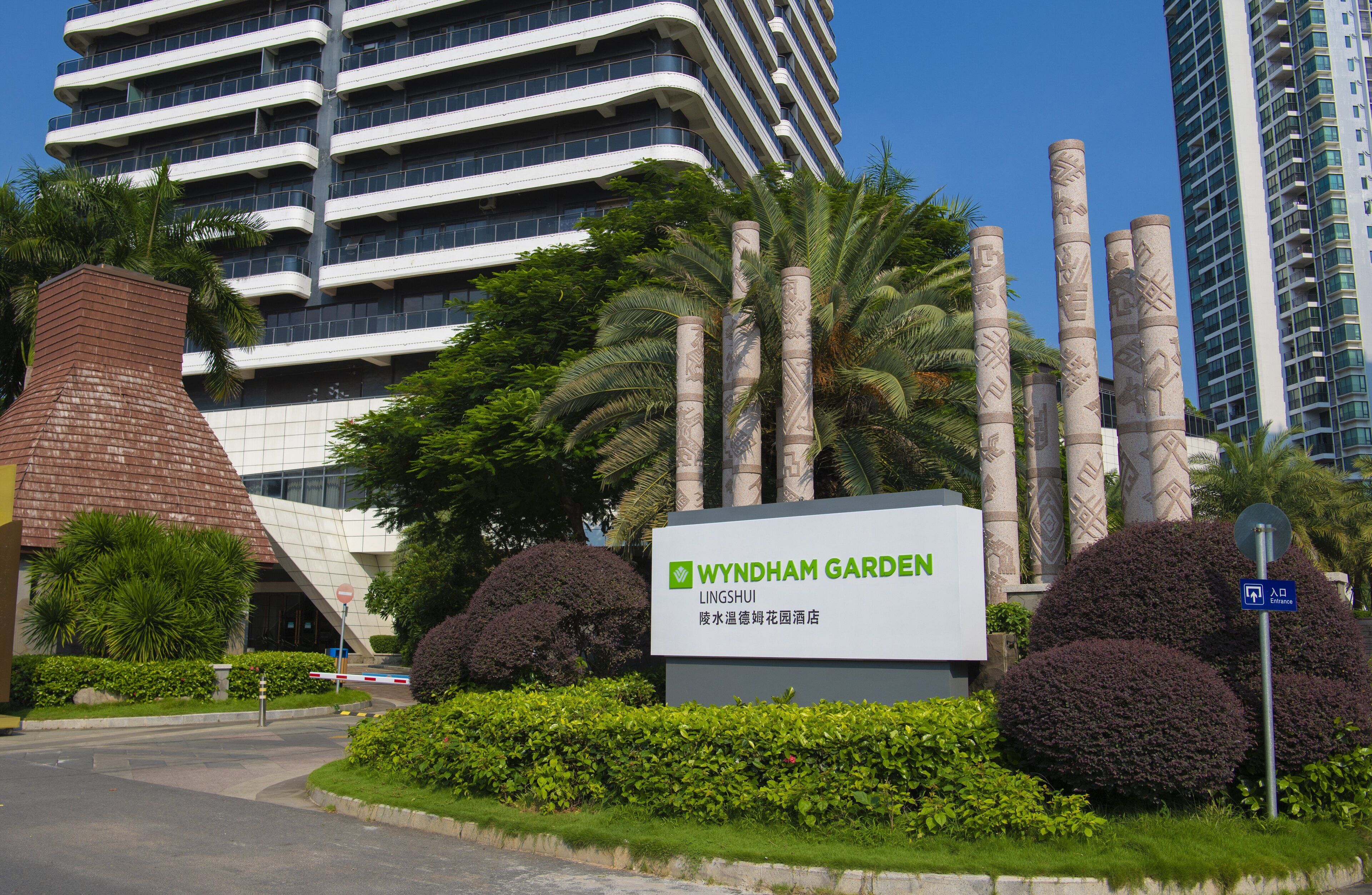 Placa para Wyndham Garden, um edifício moderno com design arquitetônico marcante, cercado por paisagismo bem cuidado e palmeiras.