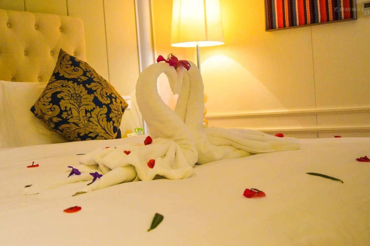 Cama com toalha em formato de cisne e pétalas de rosa.