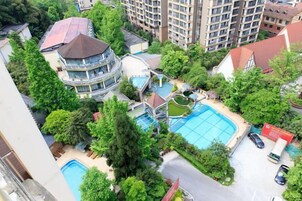 Zona residencial com piscina, rodeada por árvores e um edifício de vários andares com varandas.