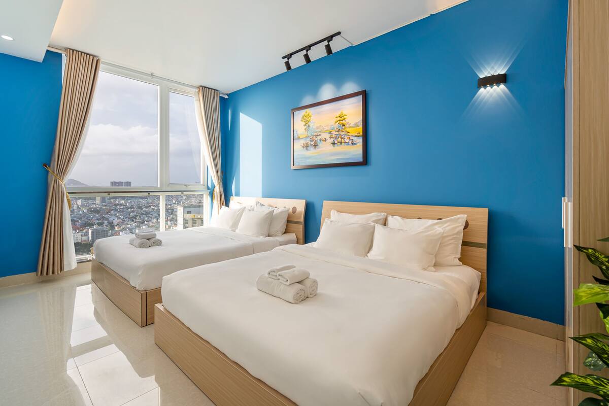 Quarto de hotel com duas camas, vista para a cidade, uma pintura e uma planta.
