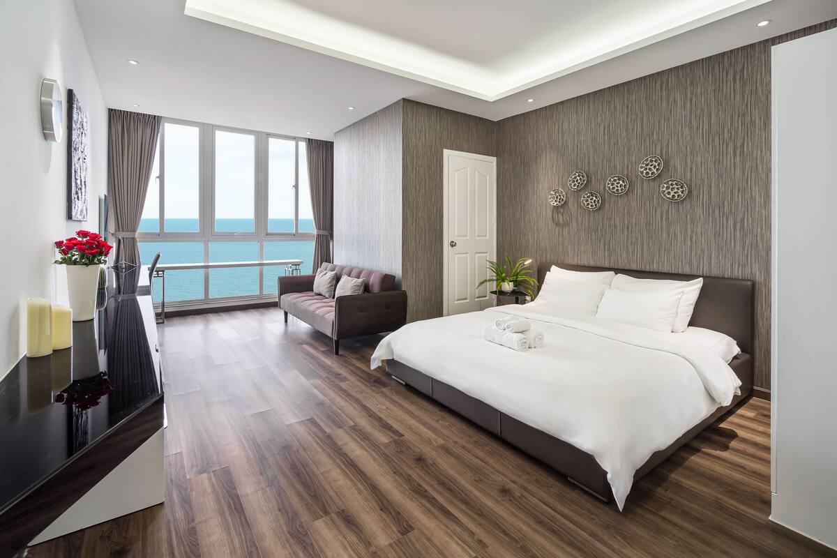 Quarto moderno com uma cama grande, um sofá e vista para o mar.