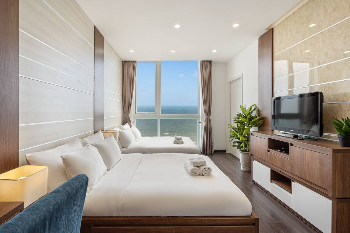 Quarto de hotel com duas camas, televisão, uma planta e vista para o mar.