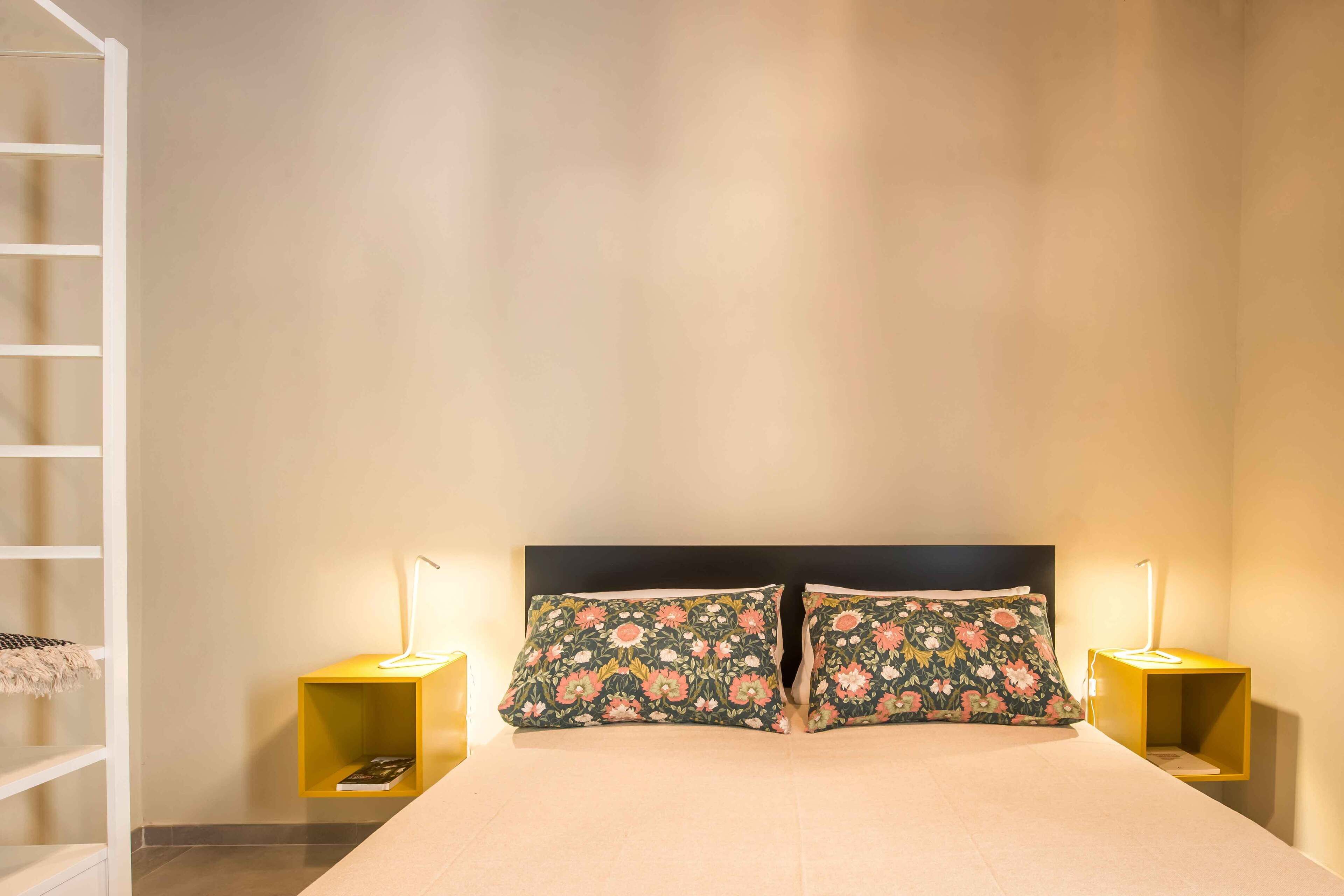 Cama bem arrumada com almofadas estampadas e duas mesas de cabeceira com luminárias.