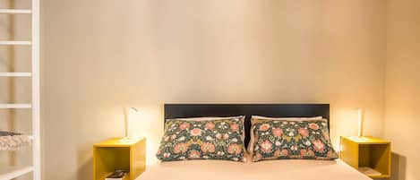 Cama bem arrumada com almofadas estampadas e duas mesas de cabeceira com luminárias.