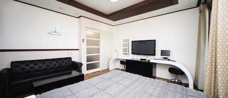 Quarto com cama, escrivaninha com televisão, guarda-roupa e sofá.