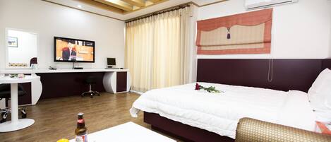 Quarto de hotel com cama, escrivaninha, cadeira, televisão e minibar.