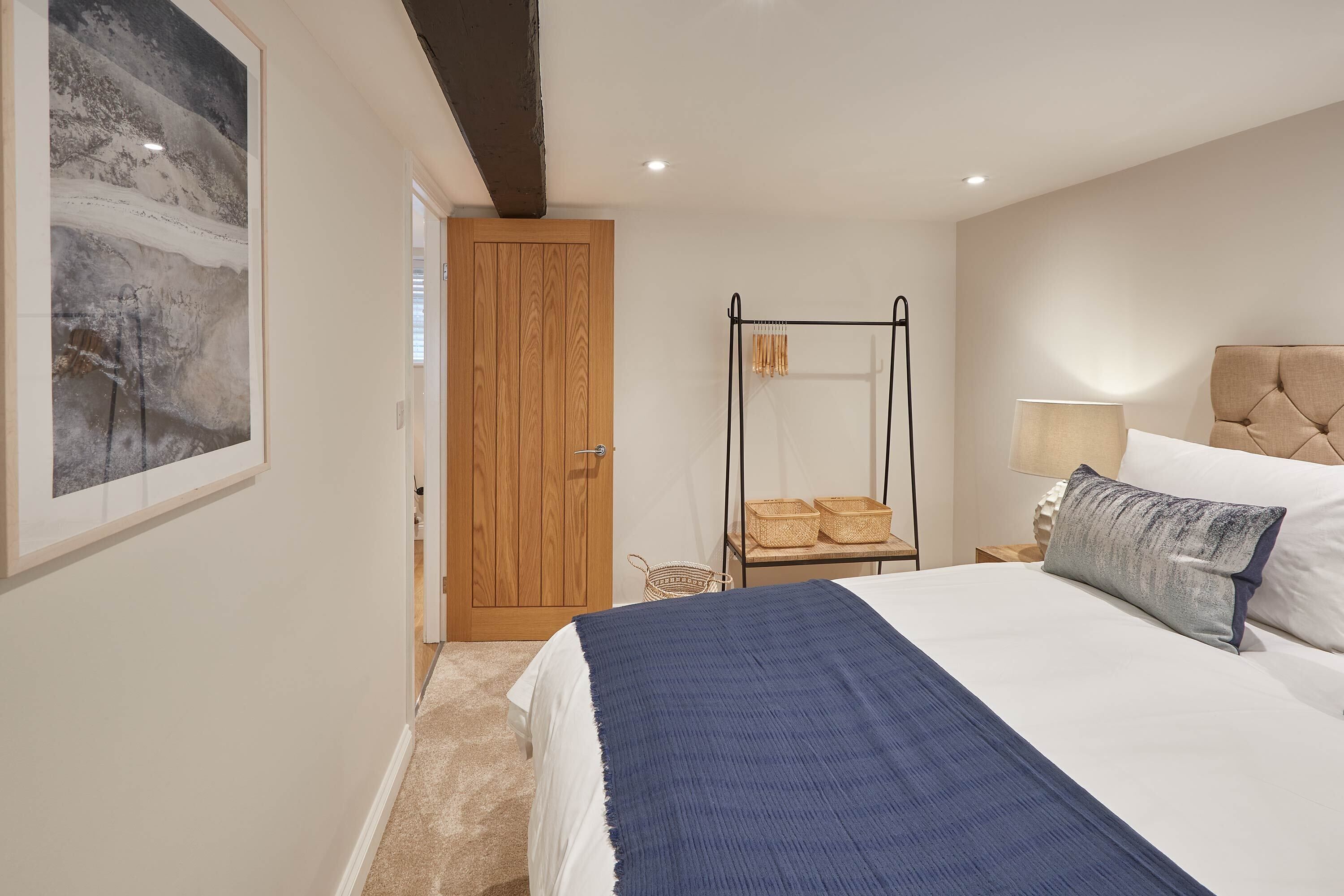 Um quarto com cama, porta de madeira, cadeira suspensa e prateleira na parede com cestos.