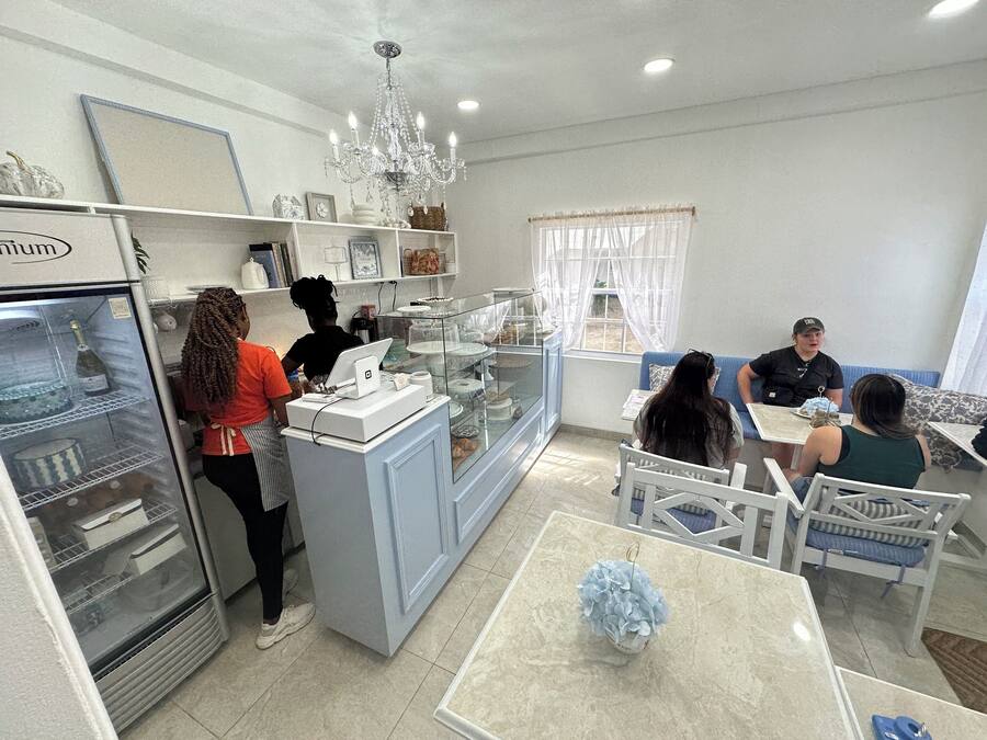 Um café com interior moderno, incluindo uma geladeira, um caixa registradora e uma área de estar com mesas e cadeiras.