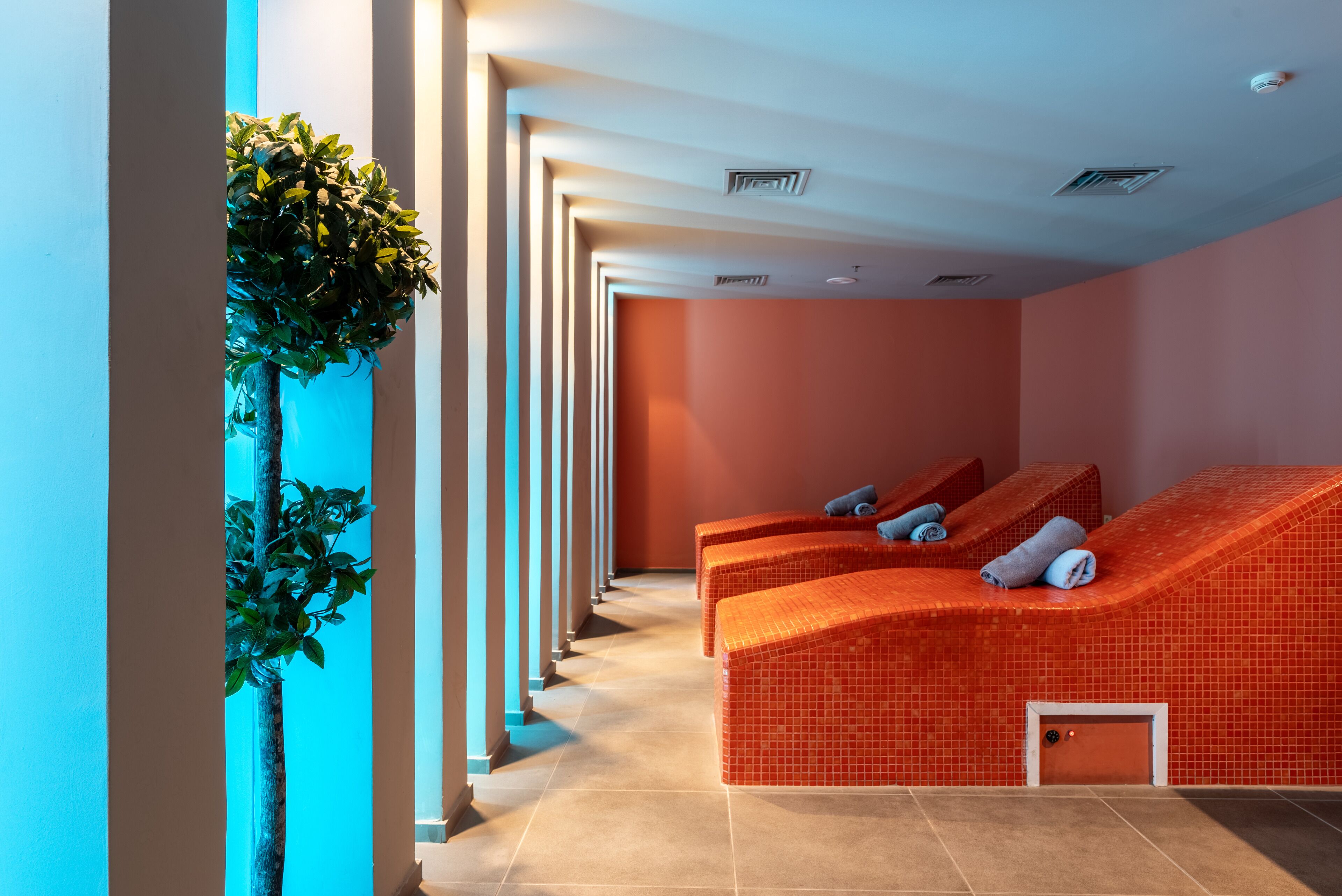 Um espaço de spa com várias macas de massagem em ladrilho vermelho, uma planta em vaso e piso ladrilhado.