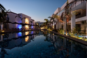 Uma área de piscina tranquila com reflexo límpido, rodeada por edifícios modernos e palmeiras.