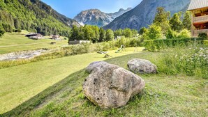 Paisagem montanhosa com uma cabana de madeira e um campo gramado.