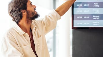 Uma pessoa apontando para um painel de informações de voos digital mostrando vários destinos e horários.