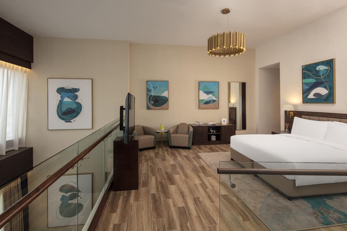 Quarto de hotel com uma cama grande, um sofá, uma mesinha e obras de arte nas paredes.